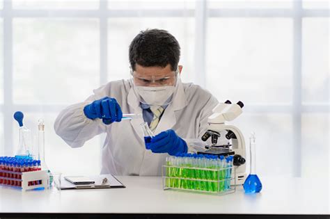 화학 시험관으로 작업하는 실험실 과학자 흰색 코트와 파란색 장갑을 착용 한 남성 연구원이 화학 분석 실험실에서 파란색 액체 샘플의 화학 튜브를 검사하고 있습니다