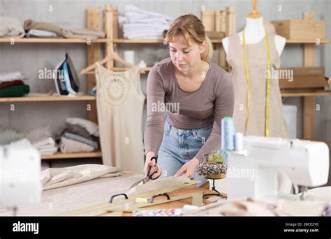 Female Dressmaker Using Fabric Shears To Cut Linen In Workshop Stock