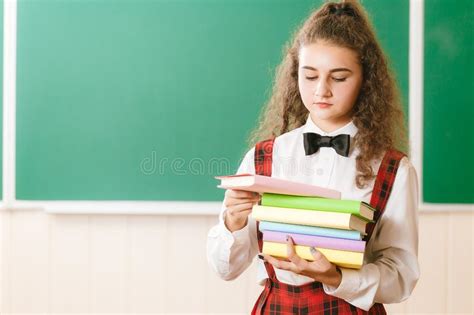 Девушка в школьной форме стоя около классн классного с книгами Студент в классе в школе Стоковое