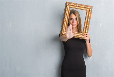 그런 지 위에 아름 다운 젊은 여 자가 심각 하 고 자신감 표현 방어 제스처 정지 표시를 하 고 오픈 손으로 빈티지 프레임을 들고 벽 그레이 액자에 대한 스톡 사진 및 기타