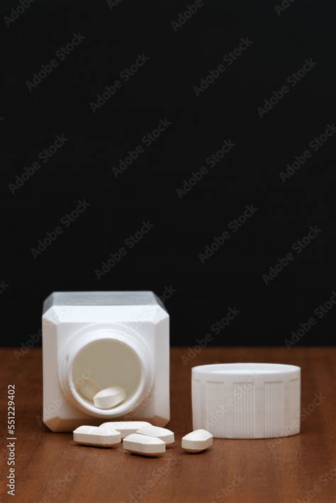 A White Open Prescription Medication Container With Some Tablets Out