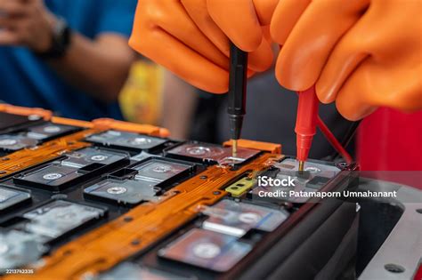 Ev의 제어 보드에 배선된 깔끔하게 배열된 Lfp 배터리 기술자는 안전 장갑을 착용한 상태에서 전압 테스터를 사용하여 혁신 충전식 배터리 안전 및 환경 보호를 강조합니다