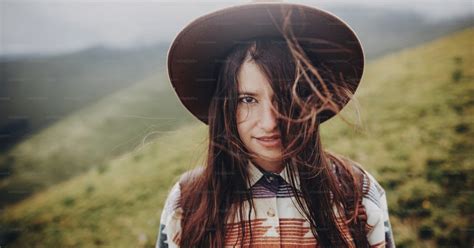 산에서 배낭 초상화를 쓴 모자를 쓴 행복한 여행자 소녀 바람이 부는 산 꼭대기에서 포즈를 취하는 힙스터 여성 텍스트 공간 방랑벽과 여행 개념 분위기 있는 서사시 순간