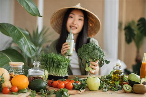 테이블에 앉아 브로콜리와 스무디를 들고 전통적인 원뿔형 모자를 쓴 아름다운 아시아 여성 생활 방식에 대한 스톡 사진 및 기타 이미지 생활 방식 절대 채식주의자 25