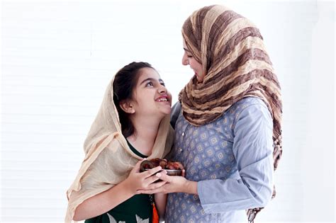 딸 딸과 함께 아름다운 아시아 무슬림 여성은 히잡 스카프와 전통 의상을 입고 서로 포옹하고 데이트 과일을 함께 들고 하얀 배경에