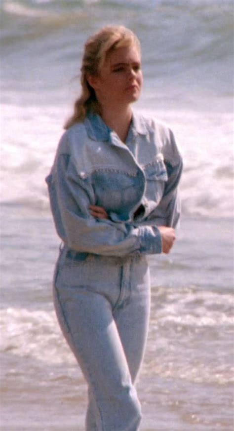 A Woman Standing On Top Of A Sandy Beach Next To The Ocean With Her Arms Crossed