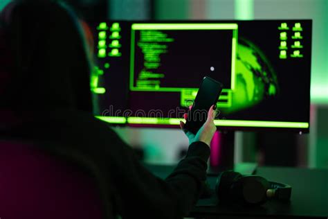Hacker Holding Smartphone In Front Of Dual Screens With Coding