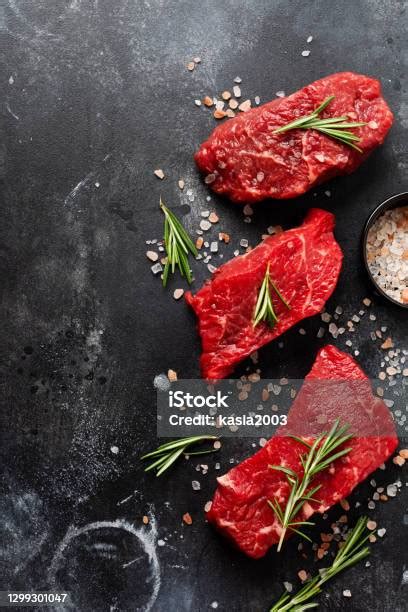 어두운 슬레이트 또는 콘크리트 배경에 향신료 양파 로즈마리와 세 개의 생 쇠고기 스테이크 위쪽 보기 가루로 빻은에 대한 스톡 사진 및 기타 이미지 Istock
