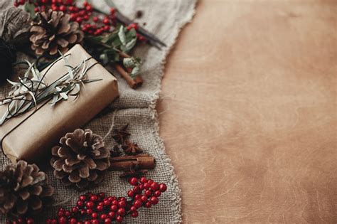 세련 된 소박한 크리스마스 선물 상자 녹색 지점 및 전나무 가지 붉은 열매 소나무 콘 소박한 나무 바탕에 계 피 간단한 에코 친화적인 현재 래핑입니다 대기 분위기 0명에