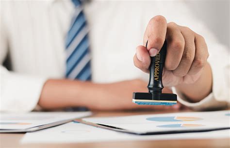 책상에서 승인된 문서에 승인된 스탬프가 찍힌 사업가의 클로즈업 비즈니스 문서 및 계약 계약 양식 용지를 확인 및 관리합니다 승인 스탬프 개념에 대한 스톡 사진 및 기타