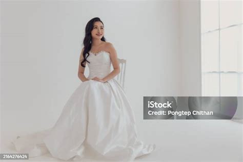하얀 웨딩드레스를 입은 예쁜 신부가 하얀 방의 의자에 앉아 있다 그녀는 얼굴에 미소를 지으며 옆을 바라본다 여자에 대한 스톡 사진 및 기타 이미지 Istock
