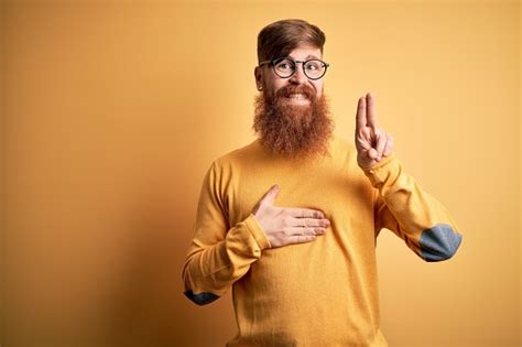 잘 생긴 아일랜드 빨강 머리 남자 수염 을 입고 안경을 통해 노란색 고립 된 배경 미소 가슴과 손가락에 손으로 맹세 충성 약속 선서만들기 남자에 대한 스톡 사진 및 기타