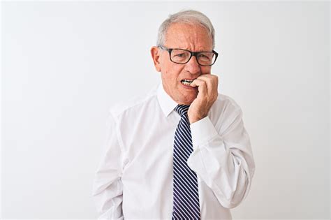 고립 된 흰색 배경 위에 넥타이와 안경을 착용한 선임 회색 머리 사업가는 손톱을 물고 입에 손을 대고 긴장하고 스트레스를 받고 있습니다 불안 문제 감정에 대한 스톡 사진 및