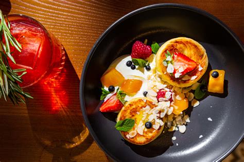 망고 딸기 라즈베리 아몬드 조각 민트 소스를 곁들인 치즈 팬케이크를 주스와 로즈마리 한 잔과 함께 테이블 위의 접시에 담아 아침 식사에 대한 스톡 사진 및 기타 이미지