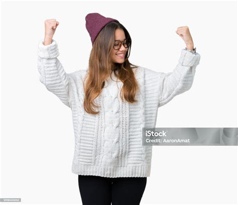 젊은 아름 다운 갈색 머리 Hipster 여자 팔 근육 자랑 웃 고 보여주는 격리 된 배경 위에 안경 및 겨울 모자를 착용 피트 니스 개념입니다 개념에 대한 스톡 사진 및