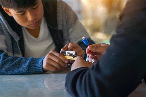 태국 소년이 전구를 직렬로 연결하고 밝기를 관찰하여 간단한 전기 회로를 연결하는 야외 과학 실험을 수행합니다 12 13세에 대한