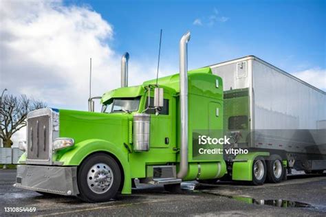 빛나는 크롬 부품과 높은 수직 배기 파이프와 다음 부하를 기다리는 주차장에 서 건조 밴 세미 트레일러와 밝은 녹색 클래식 미국