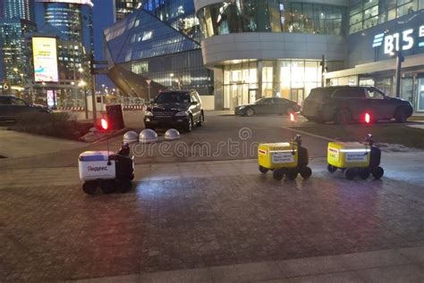Autonomous Russiaan Delivery Robots Navigating Urban Nightscape Near Modern Buildings Stock
