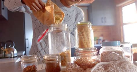 Happy African American Woman Pouring Pasta into Jar in Sunny Kitchen ...