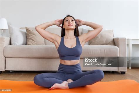 요가를 연습하는 아시아의 매력적인 미소 짓는 여자 하프 로터스 운동에 앉아 Ardha Padmasana 포즈 운동 운동복 착용 명상 세션 실내 전체 길이 홈 인테리어 건강한