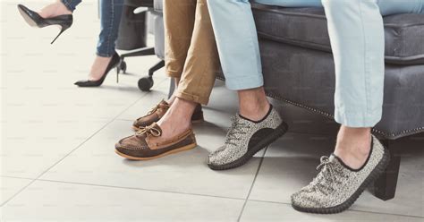 사무실 소파에 앉아 있는 젊은 남자들과 선입선출 대기열에서 바퀴 달린 의자에 다리를 꼬고 앉아 있는 여자의 다리를 닫습니다 한 남자가 무릎에 클립 보드를 가지고 있습니다