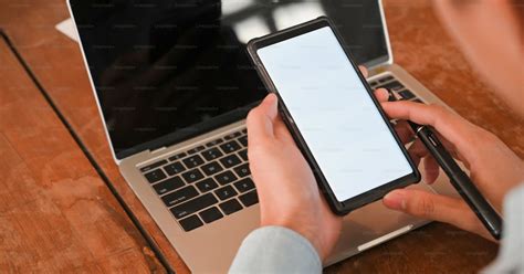 나무 작업 책상을 배경으로 노트북 앞에 펜과 흰색 빈 화면 스마트폰을 들고 있는 사업가의 자른 사진 사진 Unsplash의 태국 이미지