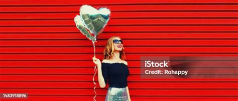빨간 배경에 은색 하트 모양의 풍선으로 포즈를 취하는 아름다운 행복한 미소를 짓는 젊은 여성의 초상화 25 29세에 대한 스톡