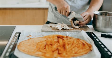 현대 흰색 부엌에서 피자를 위해 케첩으로 둥근 반죽을 배경으로 버섯을 자르는 사람 홈 피자를 만드는 과정 재료가 닫힙니다