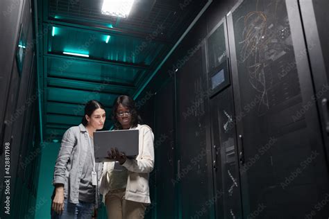 Waist Up Portrait Of Two Female IT Engineers Setting Up Server Network Via Laptop While Working