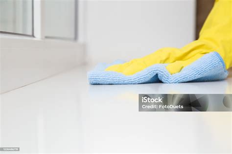 파란색 마른 헝겊으로 먼지에서 흰색 플라스틱 창틀을 닦아 노란색 고무 보호 장갑에 청소기 손 일반 또는 일반 정리 청소 서비스 근접 촬영 낮은 각도보기 관리인에 대한 스톡