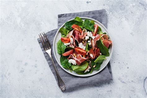 시금치 체리 토마토 모짜렐라 소나무 견과류 햄을 곁들인 봄 샐러드는 오래된 콘크리트 회색 배경의 간단한 세라믹 플레이트에 올리브