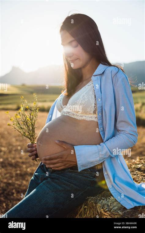 Expectant Mother In A White Lace Bra And Open Shirt Sits On A Hay Bale