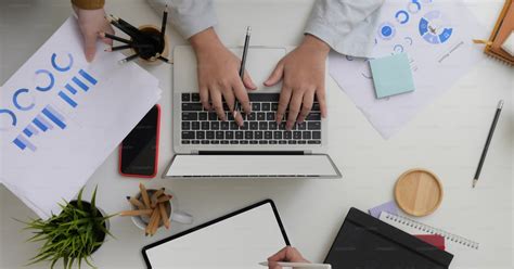 디지털 장치와 흰색 테이블에 있는 서류 작업을 사용하여 프로젝트에서 함께 작업하는 스타트업 비즈니스 팀의 오버헤드 샷 사진