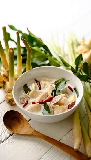 코코넛 밀크 톰 카 가이를 곁들인 세계적으로 유명한 태국 치킨 레몬그라스 카피르 라임 잎 갈란갈 말린 붉은 칠리와 함께 흰색 나무 패널 테이블 배경에 함께 그릇에 담그고