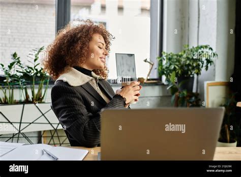 The Woman Enjoys Her Beverage Smiling Softly In Her Inviting And Green Filled Workspace Stock
