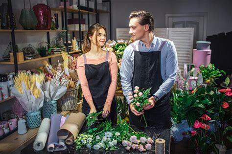 명랑 하 고 좋은 젊은 남자와 여 자가 서로 봐 그들은 테이블에 꽃다발을 확인합니다 사람들은 행복 하다 그들은 꽃과 식물의 방 채우기에서 서 있다 꽃 식물에 대한 스톡 사진