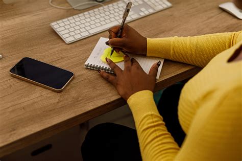 Young Woman Sitting At Her Desk Writing Down Notes While Working Stock