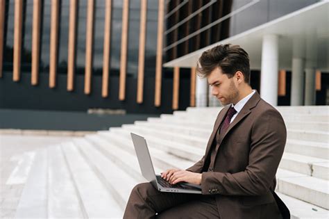 스타일리시한 양복을 입은 집중적인 사업가가 도시 환경에서 원격으로 계단을 밟고 노트북으로 타이핑하고 화면을 보는 데 집중하는 측면 모습 25 29세에 대한 스톡 사진 및