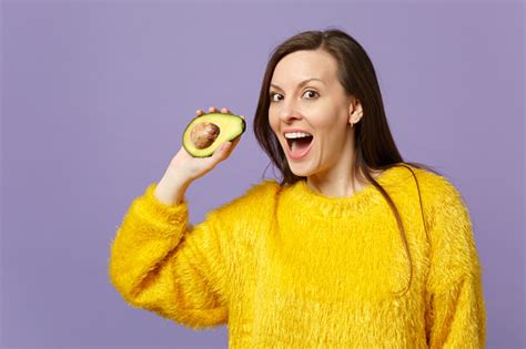 모피 스웨터에 흥분 젊은 여자는 보라색 파스텔 배경에 고립 된 신선한 잘 익은 녹색 아보카도의 절반을 유지 입 오픈 사람들은