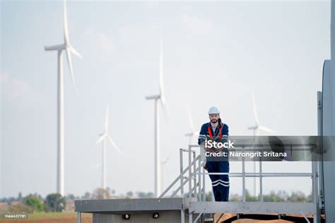 엔지니어 또는 기술자 작업자는 풍차 또는 풍력 터빈의 바닥에 서서 푸른 하늘이 있는 배경의 풍차 클러스터 앞에 카메라 스테이를 봅니다 20 24세에 대한 스톡 사진 및 기타