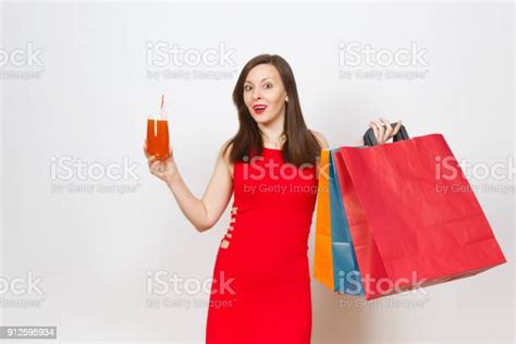 매력적인 글 래 머 칵테일 음료 잔을 들고 빨간 드레스 유행 젊은 여자 멀티 컬러 패킷을 구입 흰색 배경에 고립 쇼핑 후 광고에 대 한 공간을 복사 합니다 가방에 대한 스톡