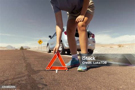 알아볼 수 없는 한 여성이 사막 도로 한복판에서 차가 고장 난 후 아스팔트 위에 빨간 경고 삼각형 표지판을 놓고 있다 거리에 대한 스톡 사진 및 기타 이미지 Istock