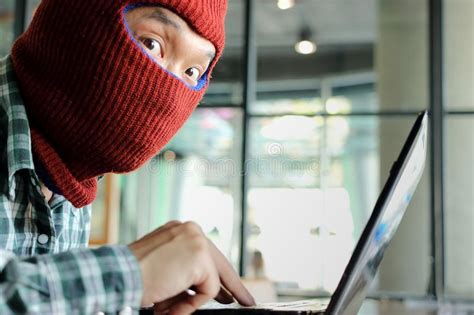 Masked Hacker Wearing A Balaclava Using Laptop Stealing Important Information Data Internet