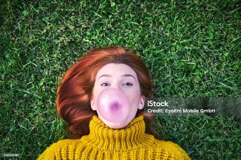 Portrait Of Woman Blowing Bubble Gum While Lying On Grassy Land Stock