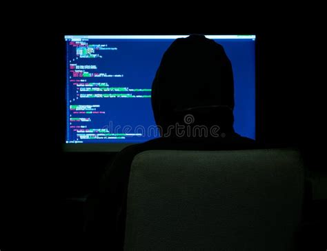 Programmer In Hoodie And Sunglasses Hacking Passwords On Laptop Sitting At A Desk In A Dark Room