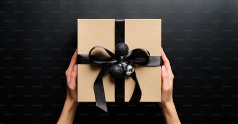 골판지 선물 상자를 들고 있는 여성 손은 검은 바탕에 검은 리본과 크리스마스 공을 감쌌다 크리스마스 선물 새해 선물 상자 개념 사진 Unsplash의 묶인 활 이미지