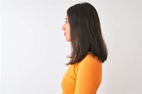 주황색 티셔츠를 입은 젊은 아름다운 중국 여성이 고립된 흰색 배경 위에 서서 옆으로 바라보며 자신감 있는 미소로 자연스러운 얼굴로 프로필 포즈를 취합니다 T 셔츠에 대한
