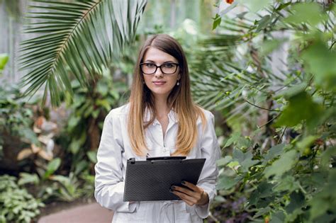 온실 과 열대 식물 온실에서 자라는 식물을 검사하고 클립 보드를 들고 메모를 만드는 동안 젊은 매력적인 백인 여성 과학자가