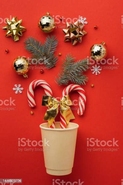 사탕 지팡이로 가득 찬 일회용 종이컵과 황금 크리스마스 트리 장난감으로 장식된 크리스마스 배경 커피 한 잔 개념입니다 빨간색 배경입니다 플랫 레이 금색에 대한 스톡 사진 및