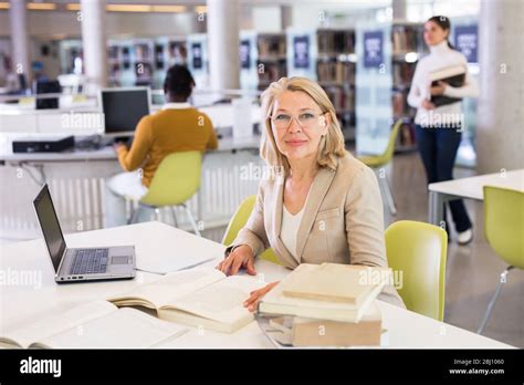 Portrait Of Positive Mature Woman With Book In Public Library Stock